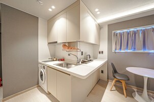 Uma cozinha compacta com máquina de lavar embutida, pia e pequena área de refeições com mesa e cadeira.