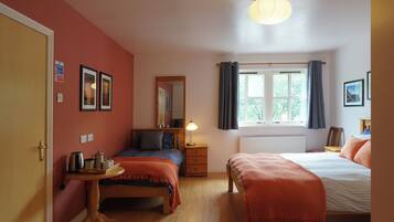 Quarto com duas camas, uma mesa, uma luminária, uma janela com cortinas e um radiador.