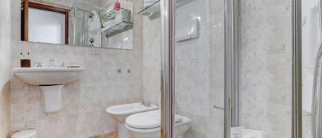 Um banheiro moderno com chuveiro em cabine de vidro, pia e vaso sanitário.
