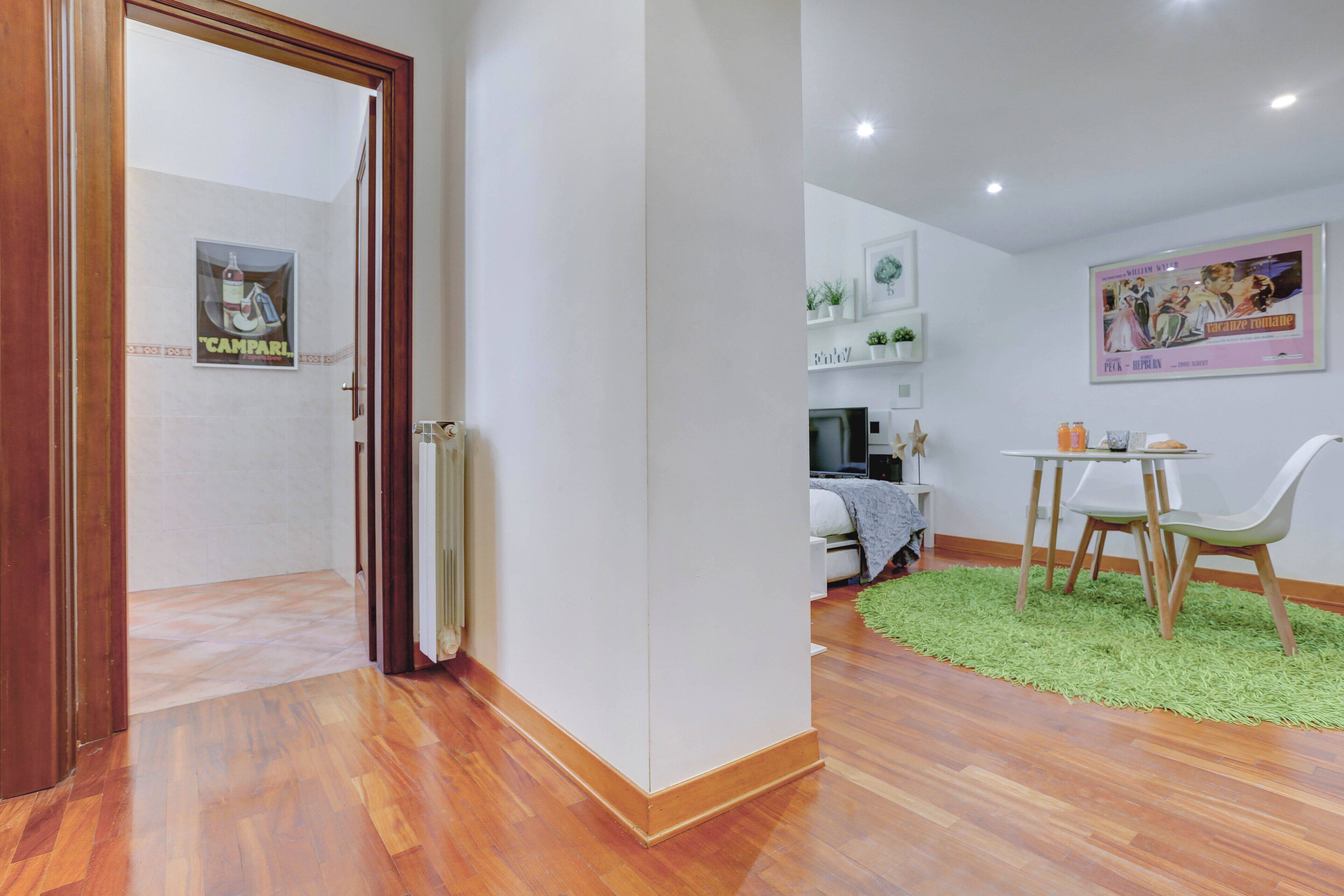 Quarto moderno com piso de madeira, um tapete verde, uma mesa de jantar com cadeiras, uma cama e um radiador.