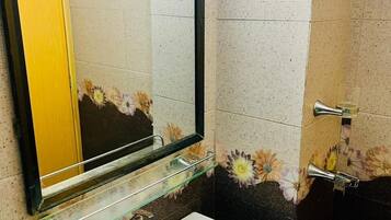 Uma casa de banho com uma pia branca, um espelho com prateleira de vidro e zona de duche.