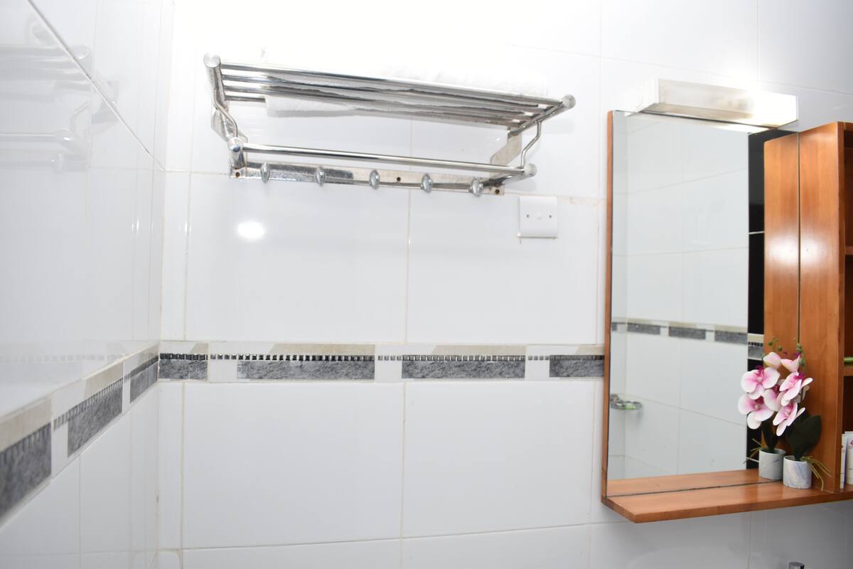 Casa de banho com azulejos brancos, um porta-toalhas cromado, uma toucador de madeira e um espelho.