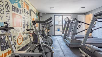 Uma academia com bicicletas ergométricas, esteiras e uma parede decorada com palavras e símbolos relacionados a exercícios físicos.