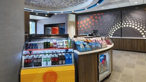 Uma área de distribuição com bebidas e petiscos, design moderno no teto, e um aviso 'COOL IT'.