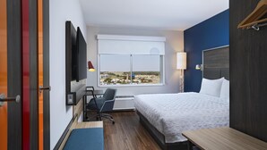 Quarto de hotel com cama, escrivaninha, cadeira, televisão e janela com vista para a cidade.