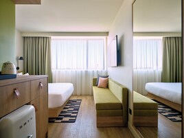 Quarto de hotel compacto com cama, sofá, escrivaninha com chaleira e espelho.