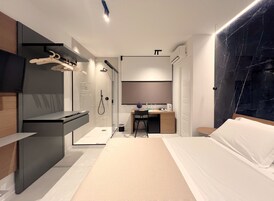 Quarto de hotel moderno com cama, escrivaninha e área de chuveiro.