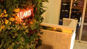 Uma mesa de recepção com um letreiro de neon que diz "ATLANTIS", rodeada por vegetação exuberante.