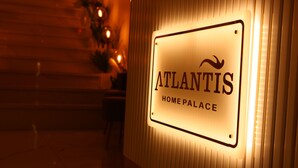 Um letreiro com o texto 'Atlantis Home Palace' e um design estilizado de onda acima do texto.