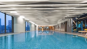 Piscina interior moderna com vista para a cidade, design de teto elegante e uma parede de vidro de um lado.