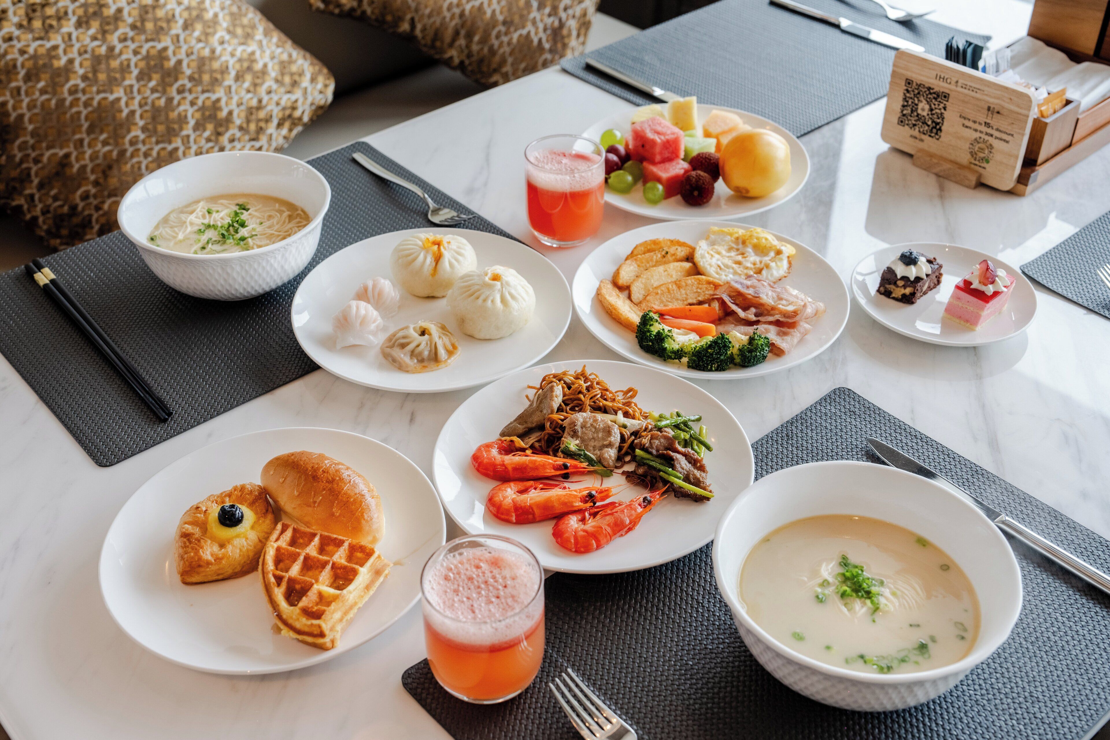 Mesa posta com diversos pratos, incluindo sopa, dumplings, macarrão, frutos do mar e sobremesas.
