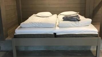 Quarto compacto com uma cama, uma mesinha e uma luminária no teto.