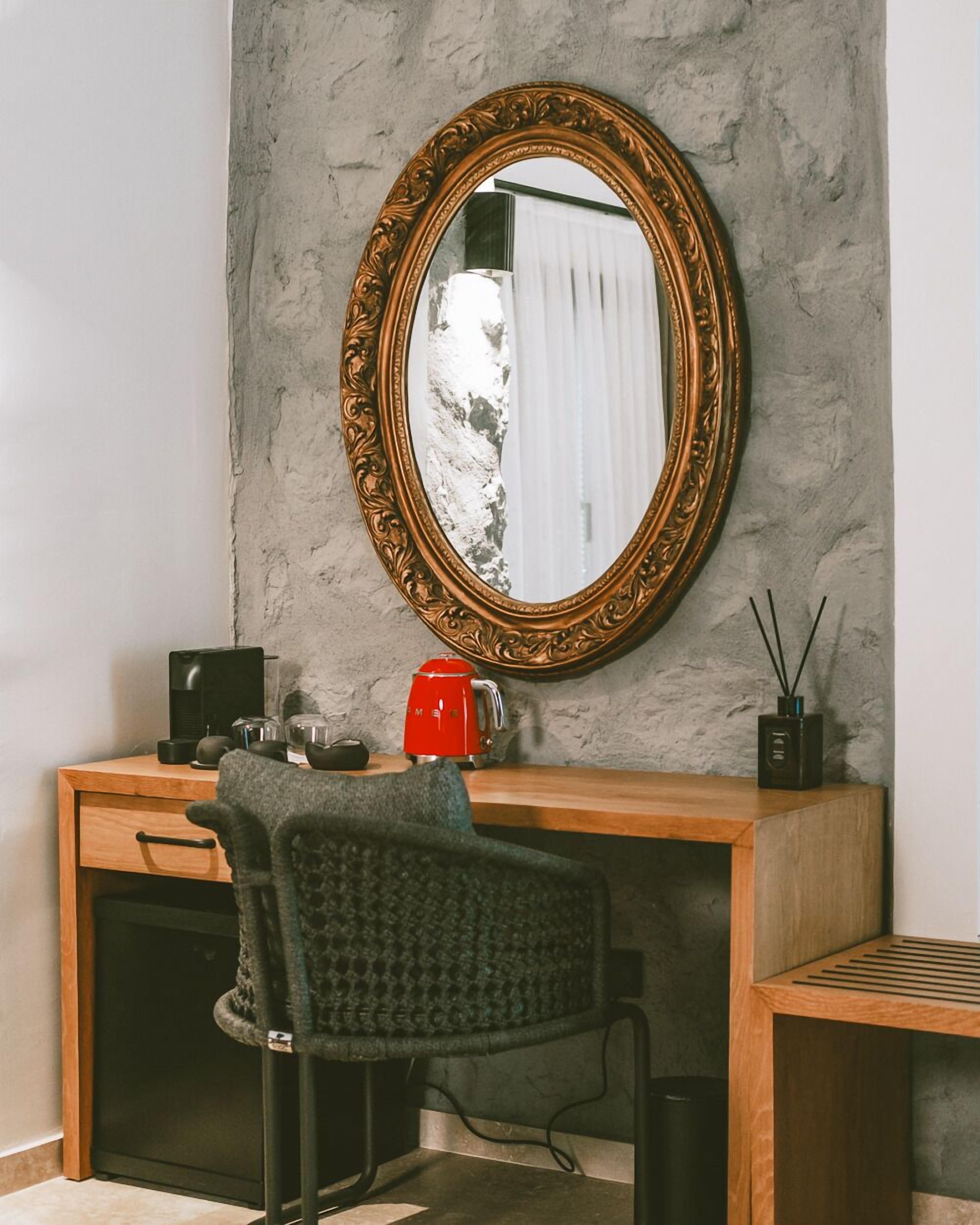 Uma escrivaninha de madeira com uma chaleira vermelha, um alto-falante preto e um espelho com moldura decorada.