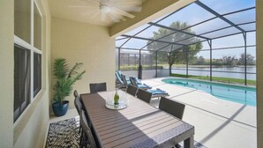 Um alpendre coberto com piscina, área de estar externa e vista para um lago.