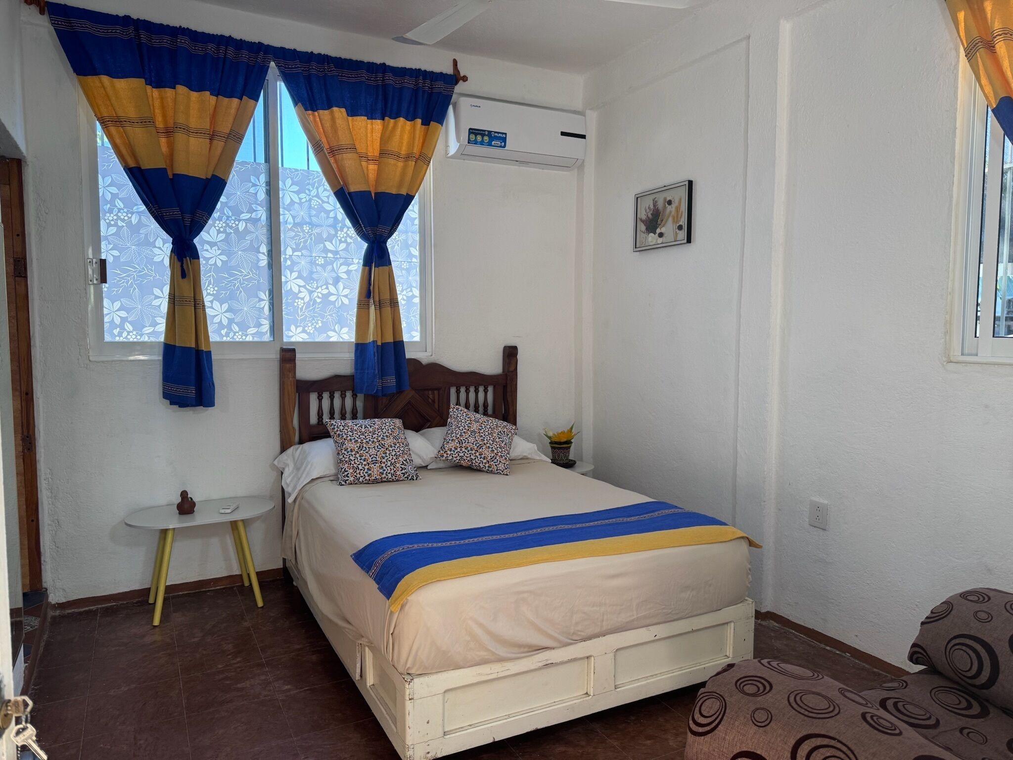 Quarto com cama, cortinas, uma mesinha e um vaso de planta.
