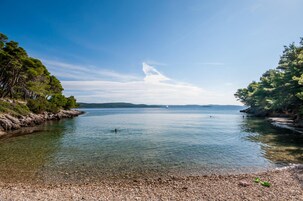 Um lago límpido com margem rochosa, rodeado por árvores e colinas ao longe.