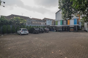 Uma área de estacionamento com vários carros, um edifício com telhado plano e uma árvore em primeiro plano.