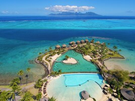 Vista aérea de um resort com várias piscinas, palmeiras e uma vista desobstruída do oceano.