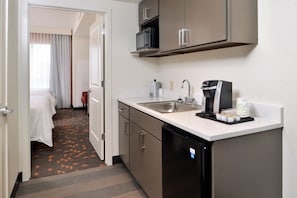 Quarto de hotel com cozinha compacta, cama, banheiro e vista para o corredor.
