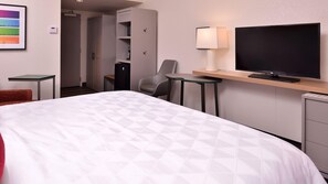 Quarto de hotel com cama, escrivaninha com televisão, cadeira, mesinha e guarda-roupa.