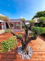 Um edifício moderno com um deck de madeira, rodeado por jardins bem cuidados e mobiliário de exterior.