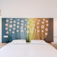 Quarto com um grande mural floral na parede, uma cama com roupa de cama branca e um telefone ao lado da cama.