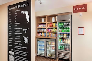 Quarto de hotel com um quadro negro exibindo informações locais sobre Altamonte Springs, FL, e uma geladeira abastecida com bebidas e lanches.