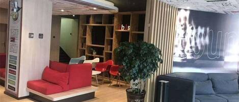 Um hall moderno de hotel com assentos vermelhos e azuis, uma grande planta em vaso e uma parede com um mapa.