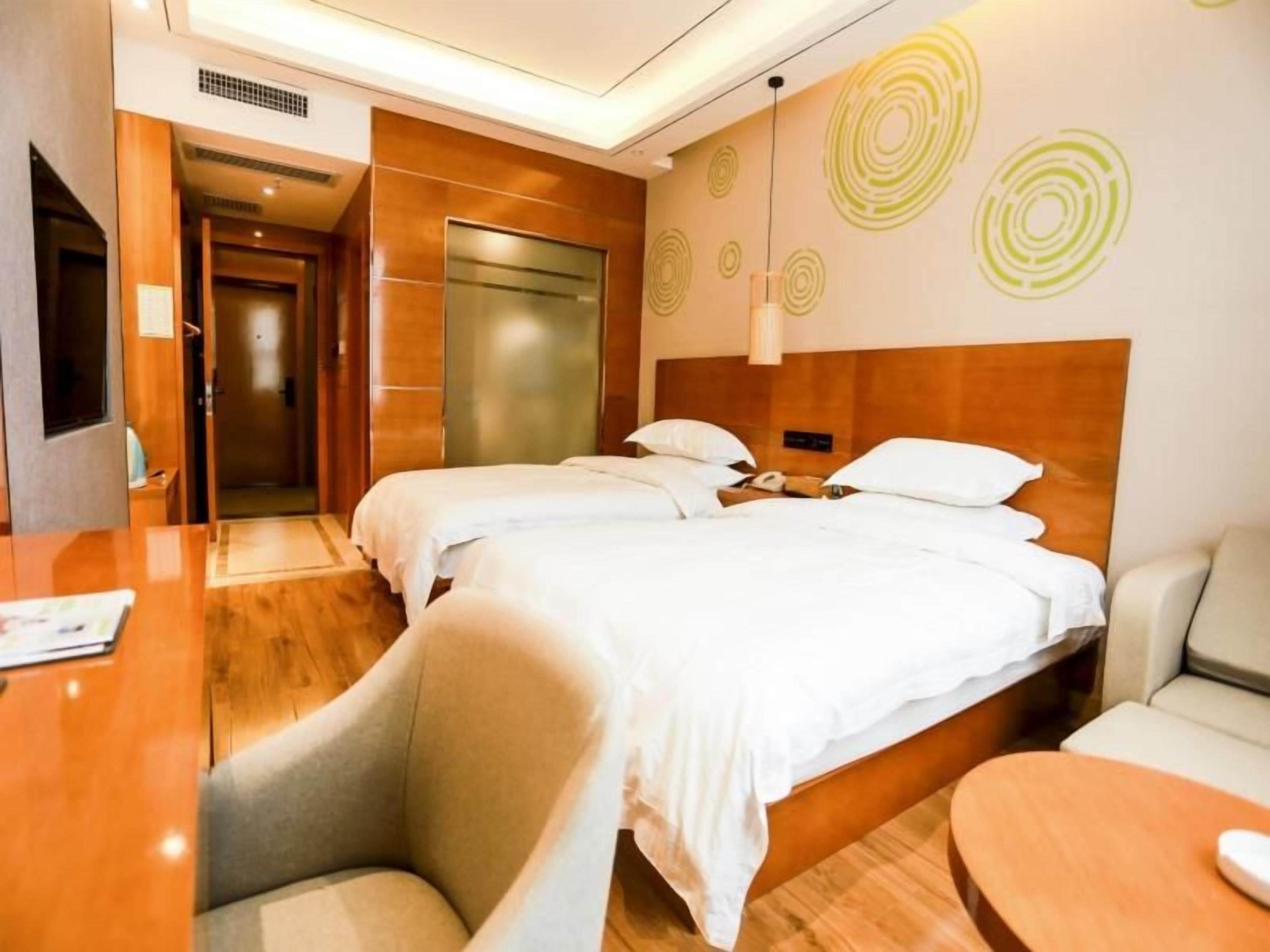 Quarto de hotel com duas camas, uma escrivaninha, uma cadeira e uma mesinha.