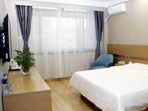 Quarto de hotel com uma cama, uma escrivaninha com uma planta, uma cadeira e um telefone na escrivaninha.