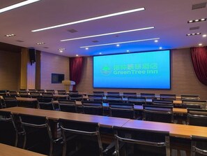 Sala de conferências com uma tela grande exibindo a marca 'GreenTree Inn', fileiras de cadeiras e uma mesa de madeira.