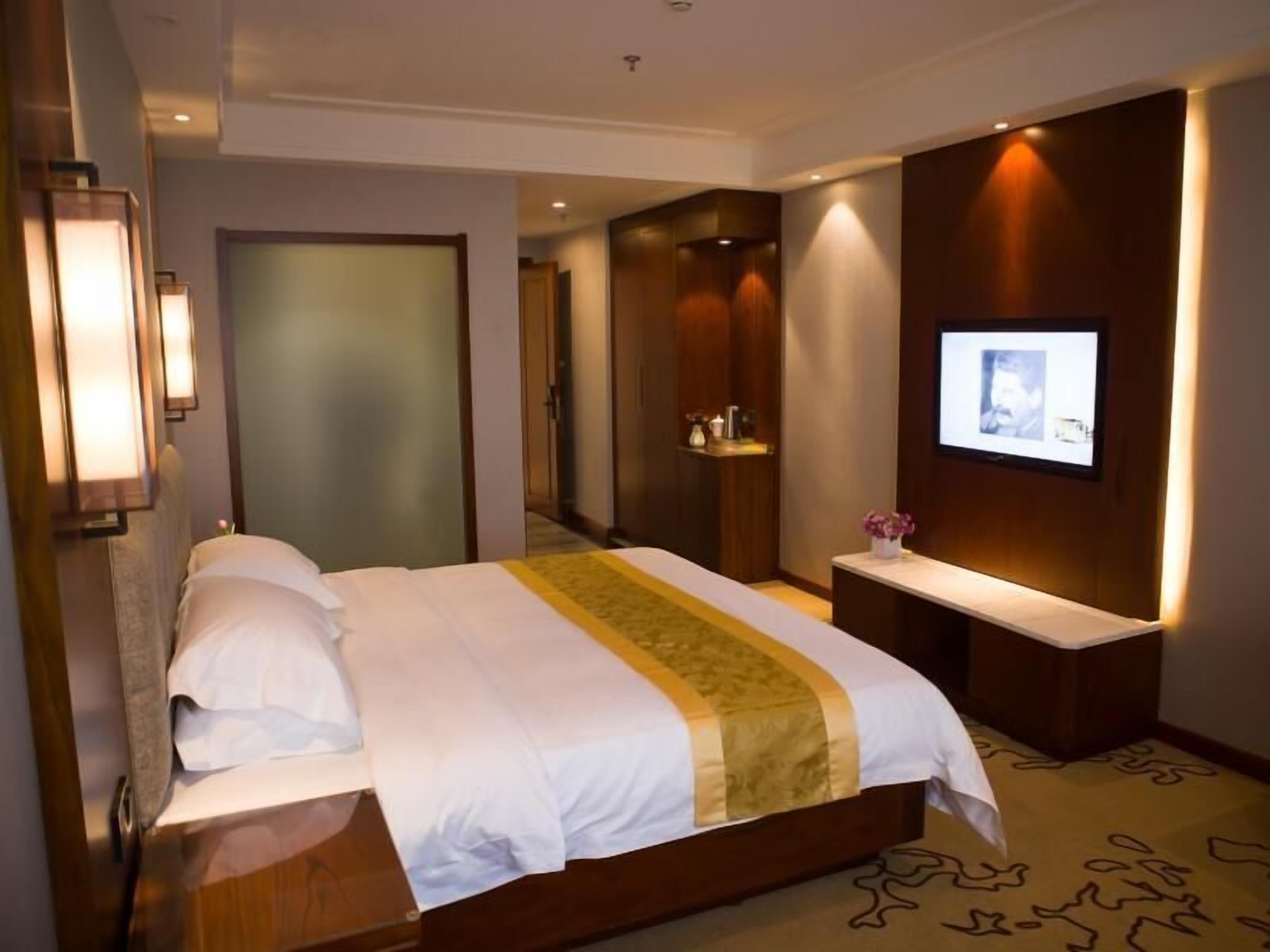 Quarto de hotel com uma cama grande, mesa de cabeceira, televisão e espelho.