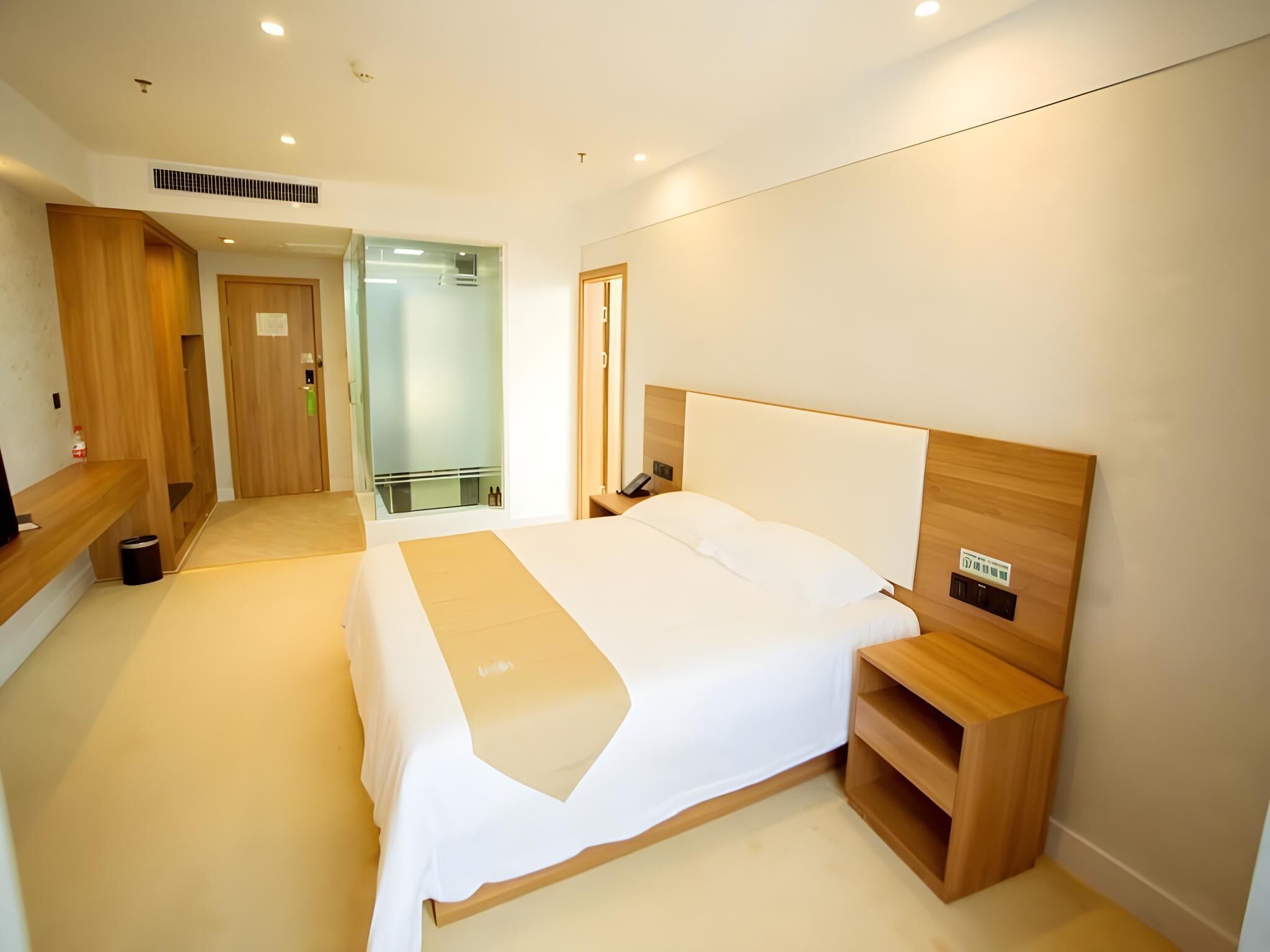 Quarto de hotel moderno com uma cama grande, cabeceira de madeira, mesas de cabeceira e um banco embutido.