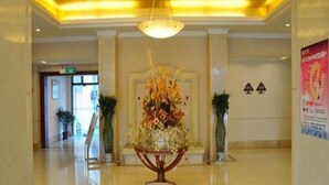 Um hall amplo com arranjo floral central, um lustre e um cartaz na parede.