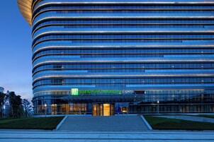 Um hotel moderno com fachada curva, grandes janelas de vidro e entrada destacada com um letreiro verde.