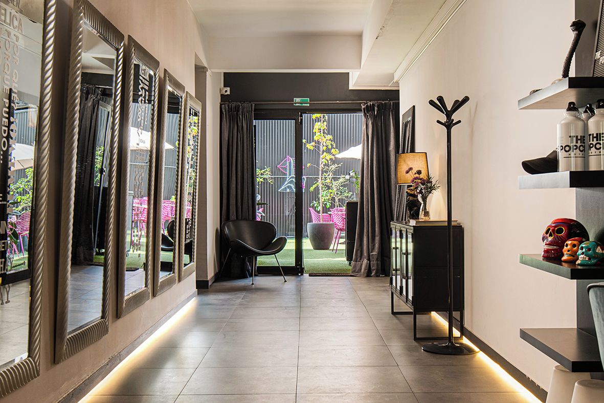 Corredor de hotel com uma cadeira, um abajur e uma estante com objetos decorativos.