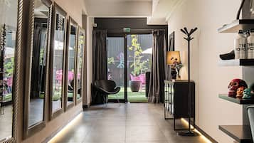 Corredor de hotel com uma cadeira, um abajur e uma estante com objetos decorativos.