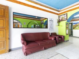 Um saguão com um sofá de couro vermelho, um espelho grande e uma parede verde com um mural.