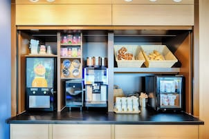 A self-service beverage station with a coffee machine, tea selection, and a refrigerator with yogurt.