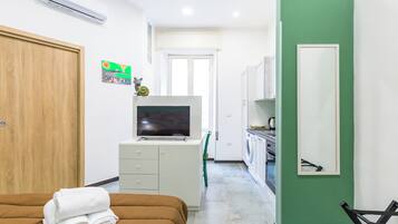Quarto de hotel com cama, televisão, guarda-roupa, parede verde e área de cozinha.