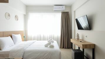 Quarto de hotel com cama, secretária, televisão e janela com cortinas.