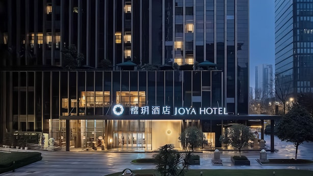 Um hotel moderno com entrada imponente, fachada bem iluminada e área externa ajardinada com assentos e elementos decorativos.