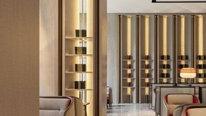Um lobby moderno com piso de mármore, área de estar com cadeiras e uma estante com prateleiras iluminadas.