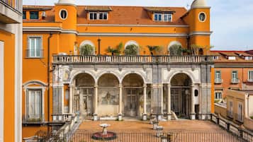 Um pátio com uma fonte, uma galeria coberta e um edifício com arcos e colunas.