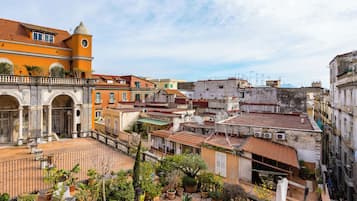 Um pátio com chão de terracota, rodeado por edifícios com varandas e plantas em vasos.