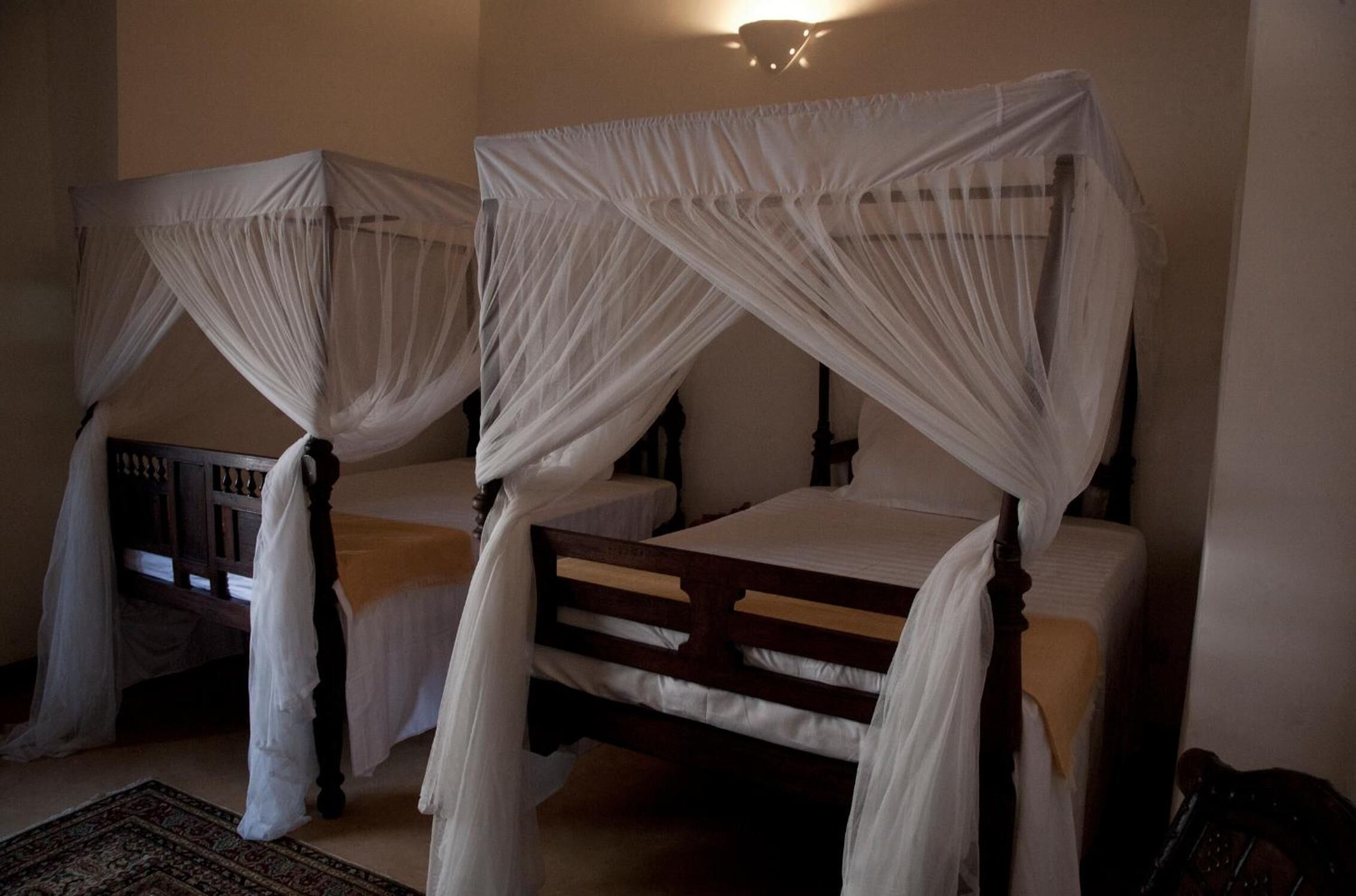 Quarto com duas camas, cada uma coberta por lençóis de dossel brancos e cortinas esvoaçantes.
