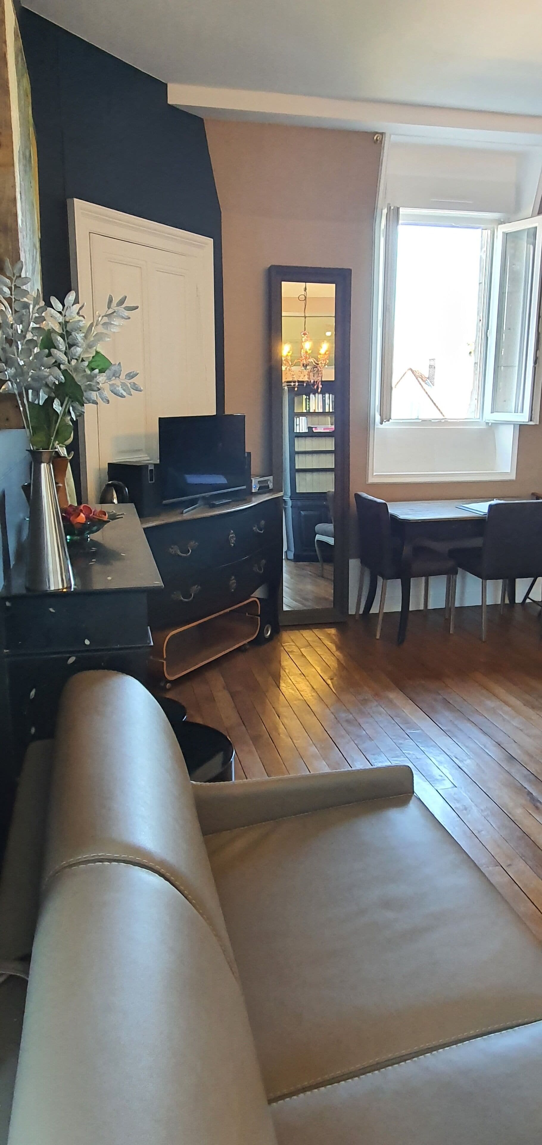 Uma sala de estar com sofá, televisão, estante de livros e um espaço de jantar com cadeiras.