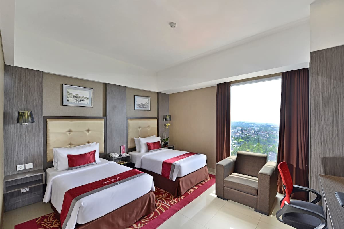 Quarto de hotel com duas camas, uma mesa, uma cadeira e uma janela grande com vista para a cidade.