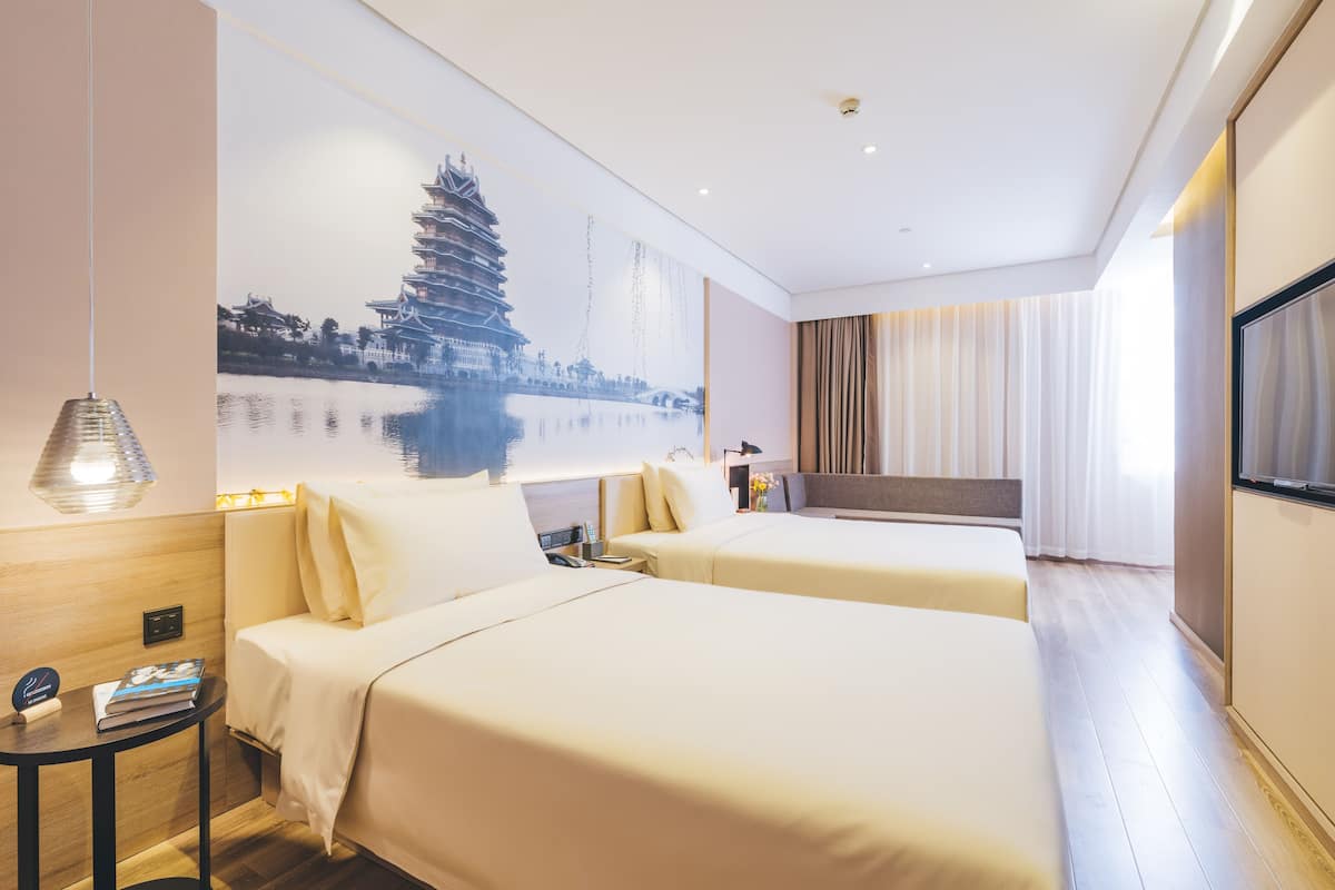 Quarto de hotel com duas camas, um grande mural na parede, uma televisão e uma pequena mesa com abajur.