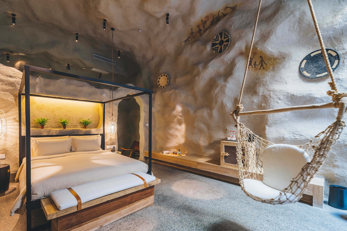Quarto com cama de dossel, cadeira suspensa e uma pequena estante com objetos decorativos.